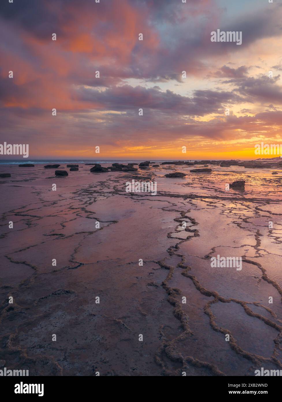 Vibrant sunset skies casting warm hues over the Atlanterra Beach rocky ...