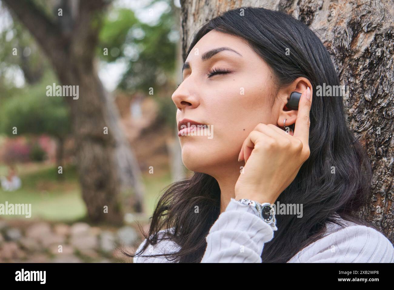 A woman leans against a tree, eyes closed and serene, enjoying the ...