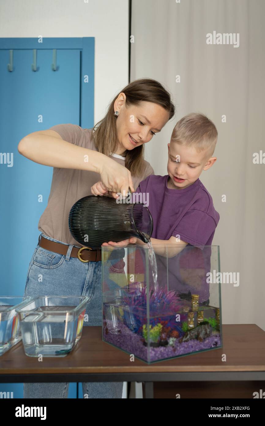 A mother and her young son are smiling as they pour water into a fish ...