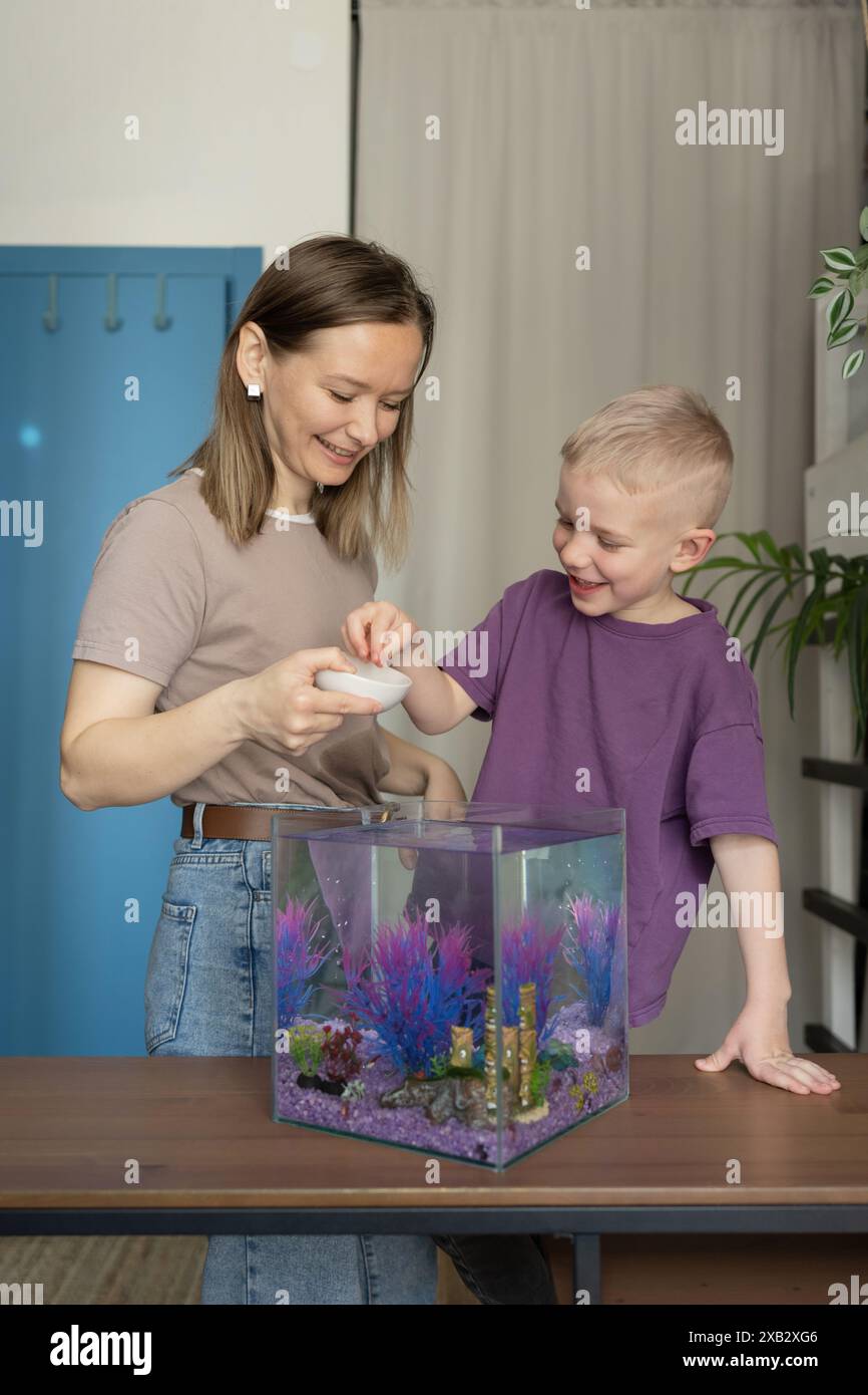 A mother and her son smile joyfully as they care for their pet fish in ...