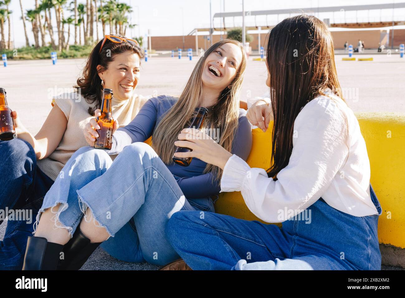 Three female friends laugh and share a relaxed moment with beers at a ...