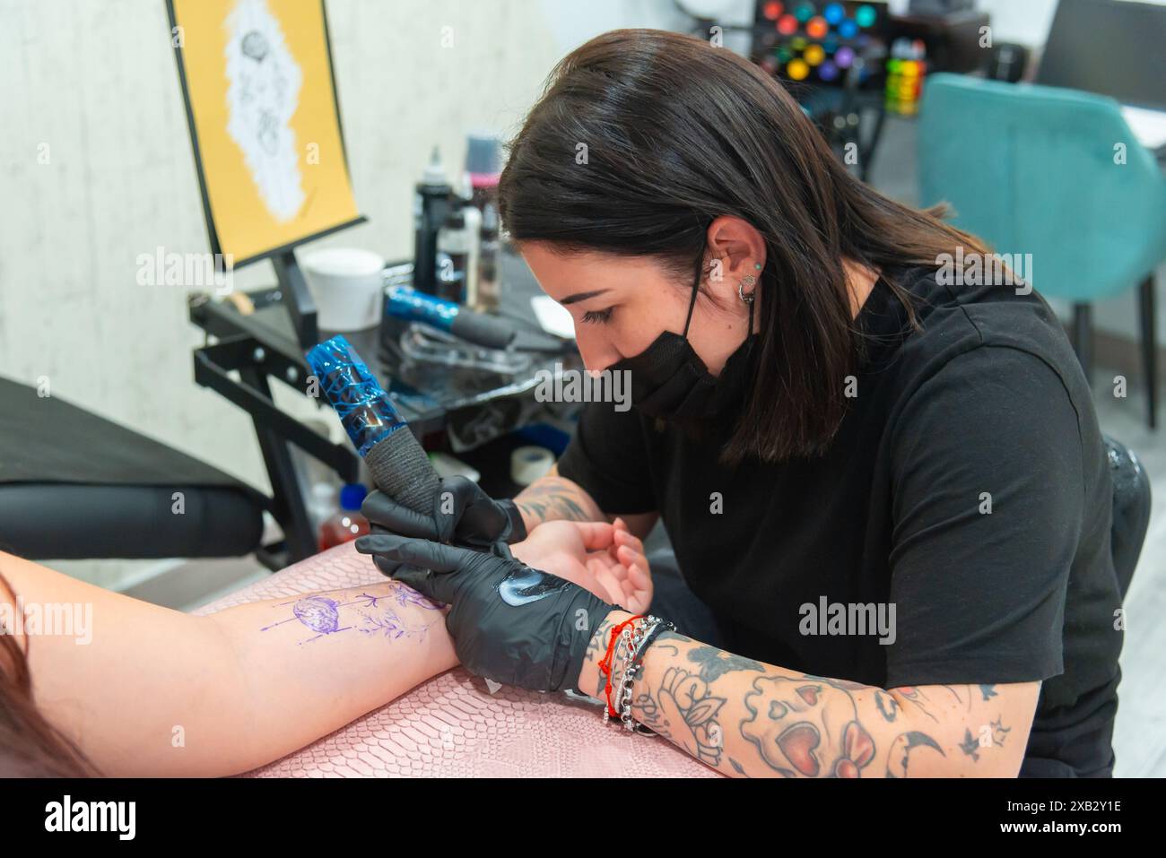 A tattoo artist with visible tattoos focuses intently on inking a ...