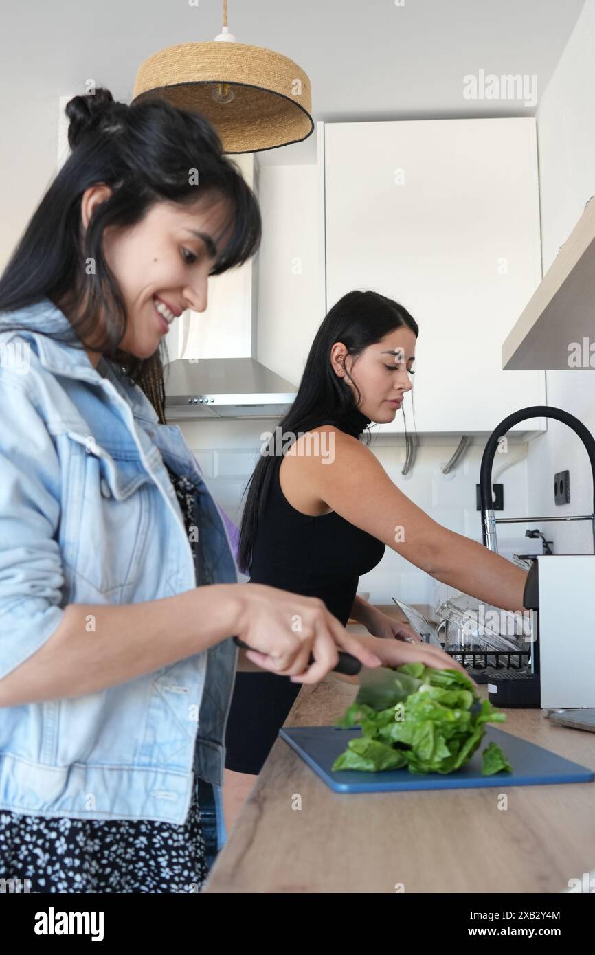 Two young women smile as they prepare a fresh salad in a well-lit ...