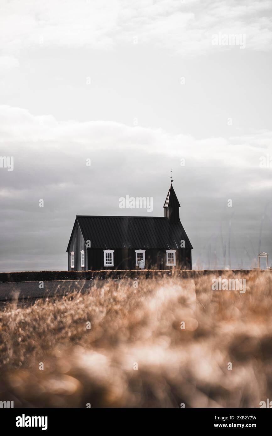 A stark black church stands in isolation among golden fields under ...