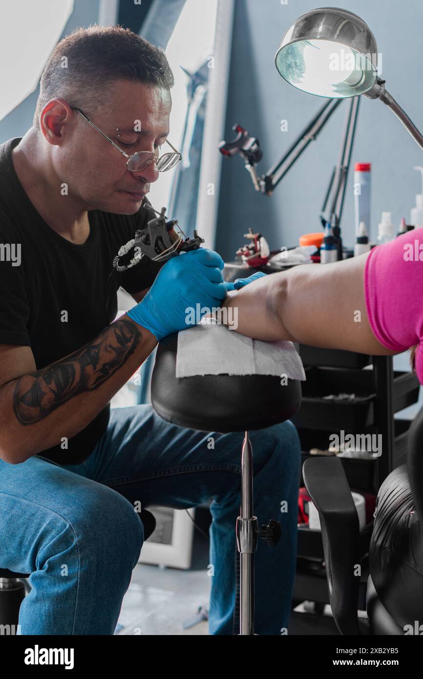 A focused Hispanic male tattoo artist skillfully inks a design on his ...