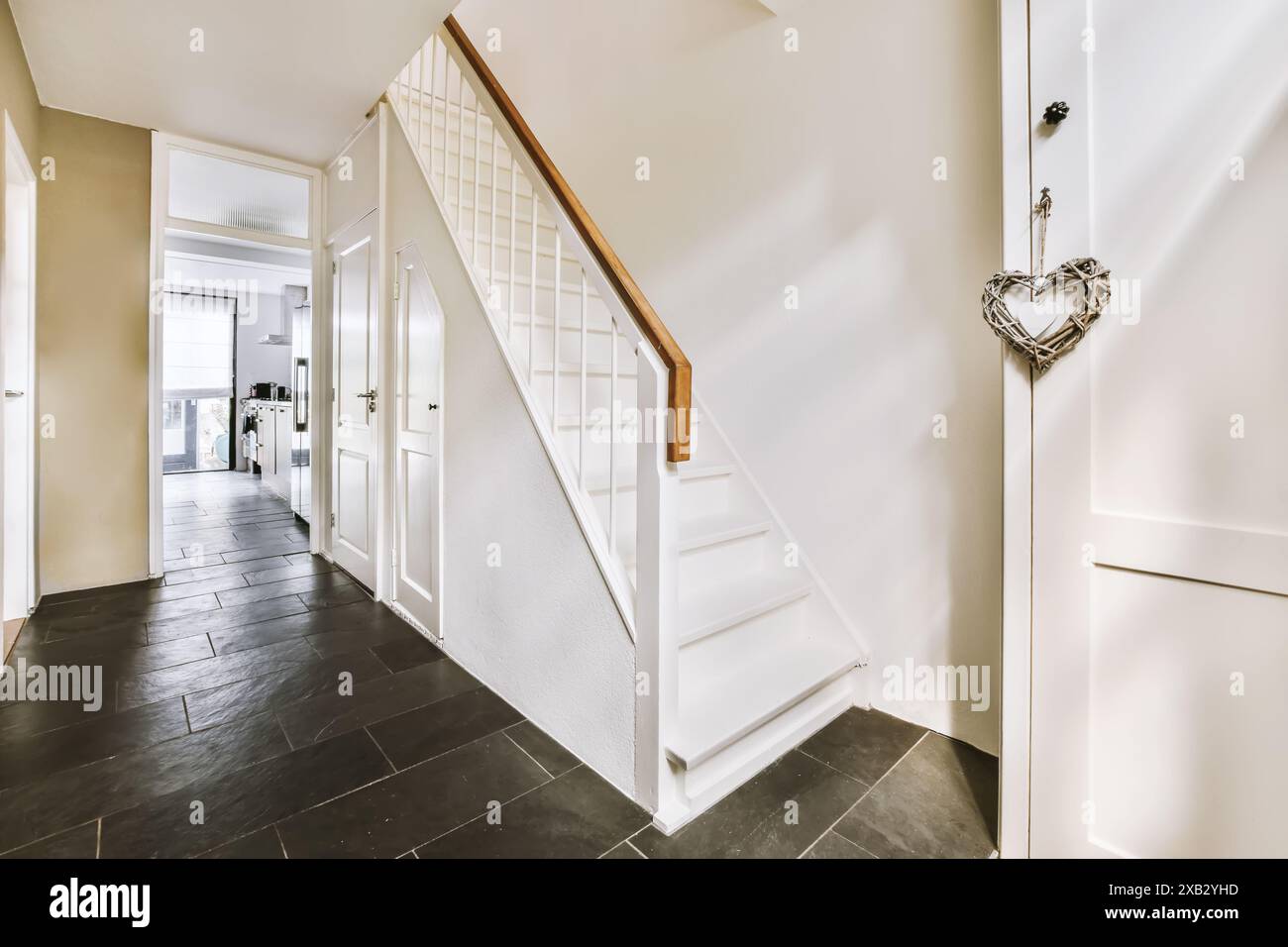 A well-lit hallway featuring a white staircase and dark floor tiles ...