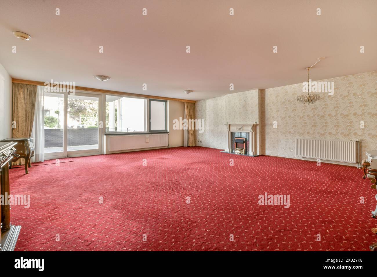 A large, empty vintage-style living room with a red carpet, patterned ...
