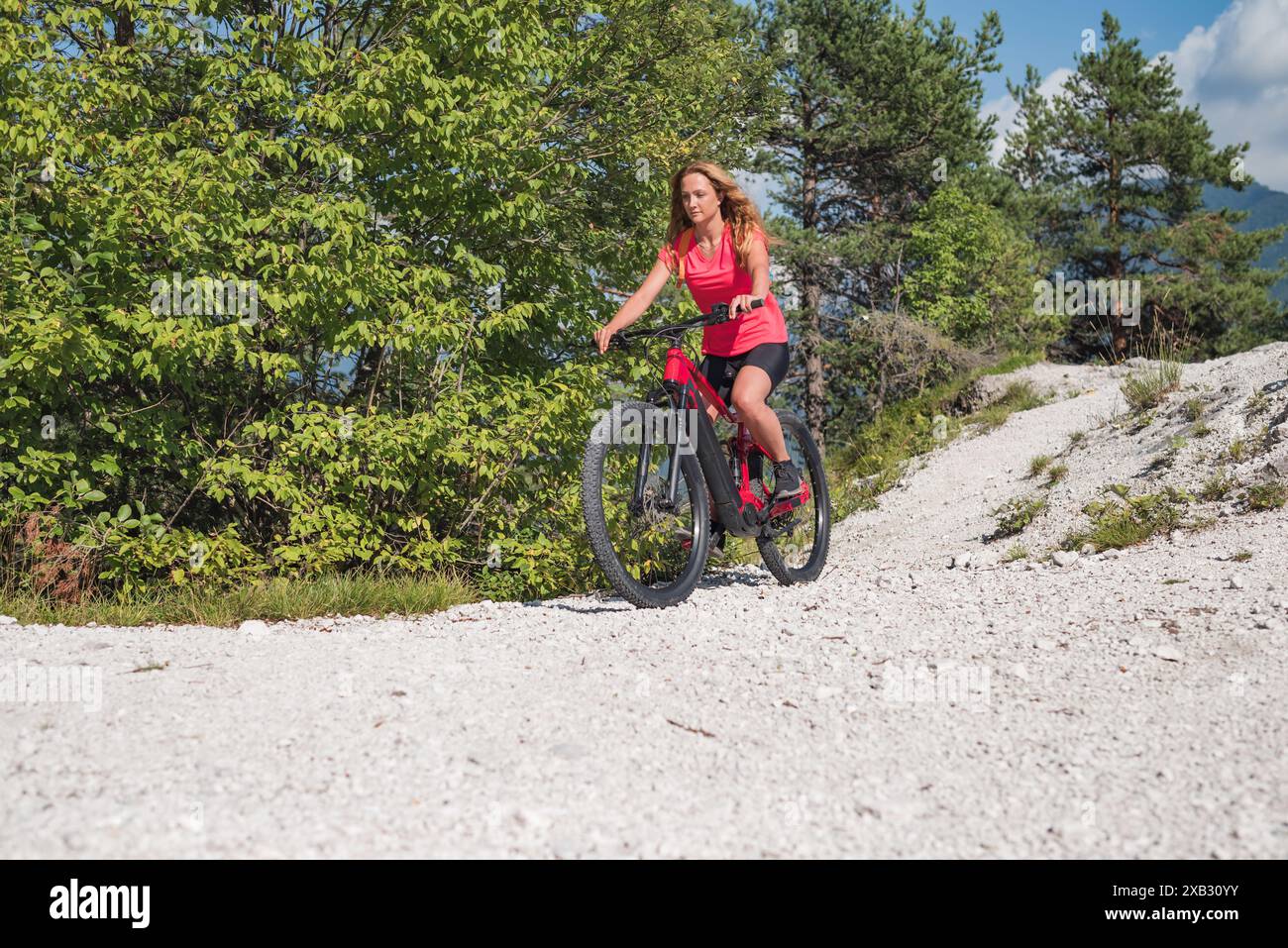 Woman without helmet on an electric mountain bike going downhill and risking head injury. Summer ...