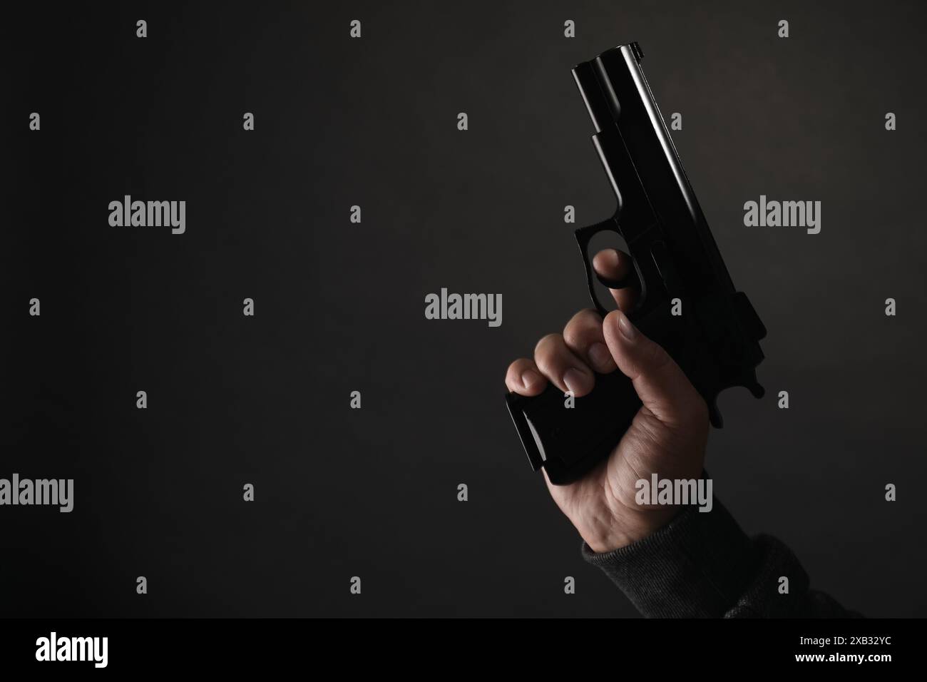 Armed robbery. Dangerous criminal with gun on black background, closeup ...