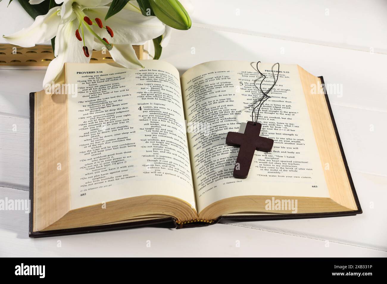 Cross, Bible and beautiful lily flowers on white wooden table, closeup ...
