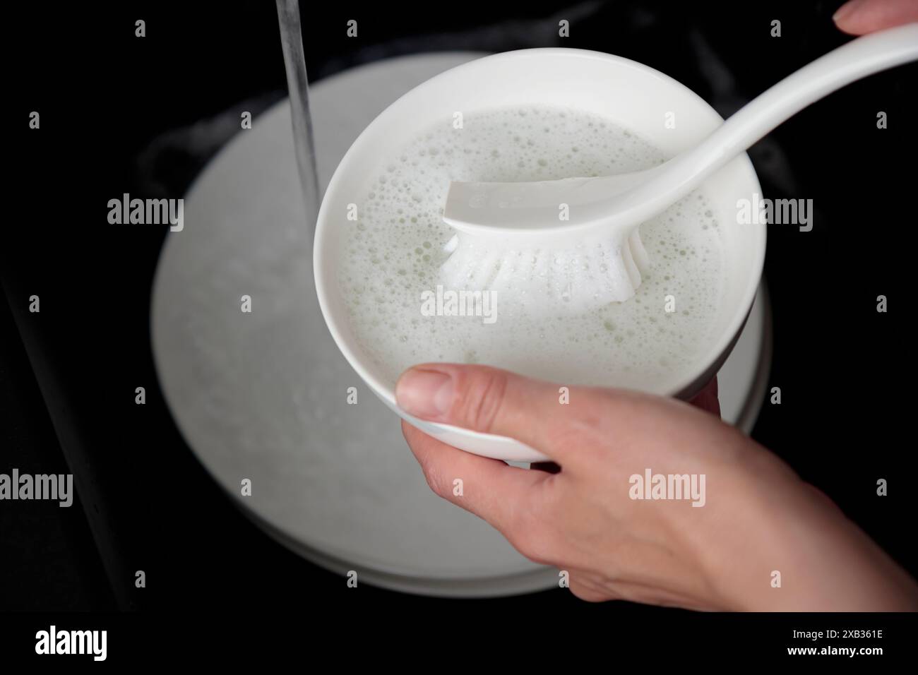 Woman washing white plates dishes with brush in the black sink ...