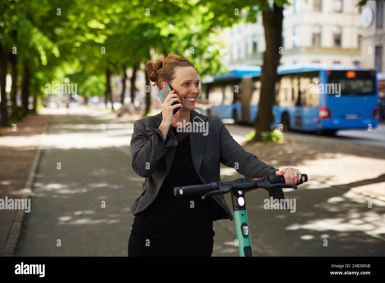 Smiling mature businesswoman with electric push scooter talking over ...
