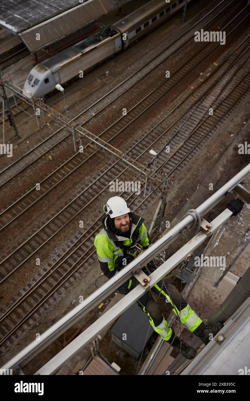 High angle view of rope access worker hanging on building by railroad ...
