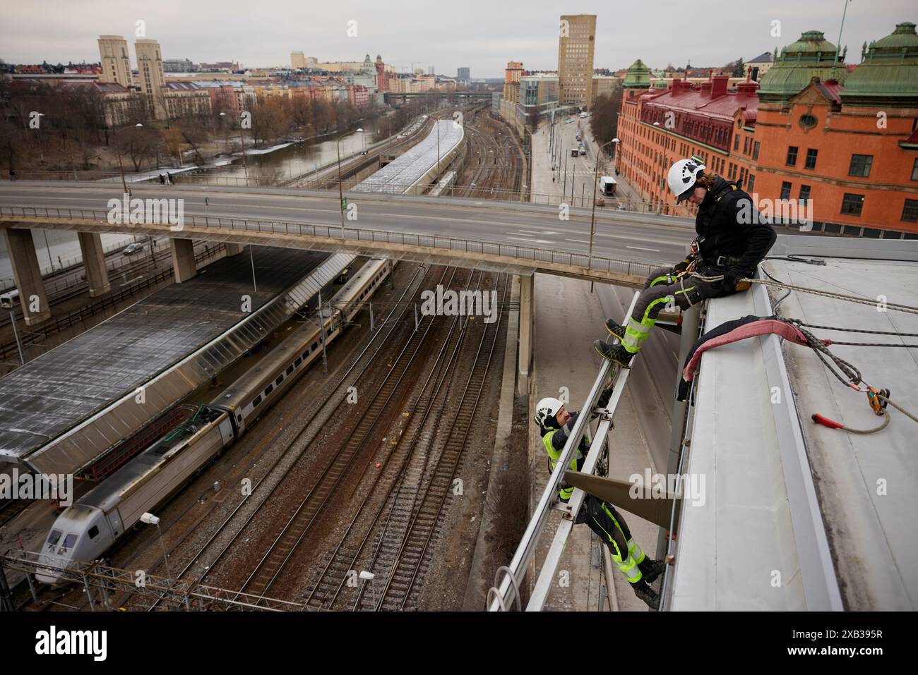 Male rope access worker with coworker hanging from building rooftop ...