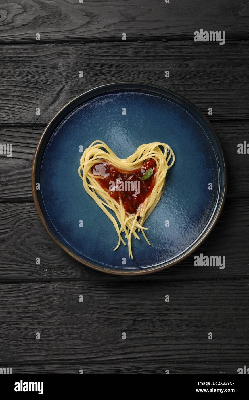 Heart made with spaghetti and sauce on black wooden table, top view ...