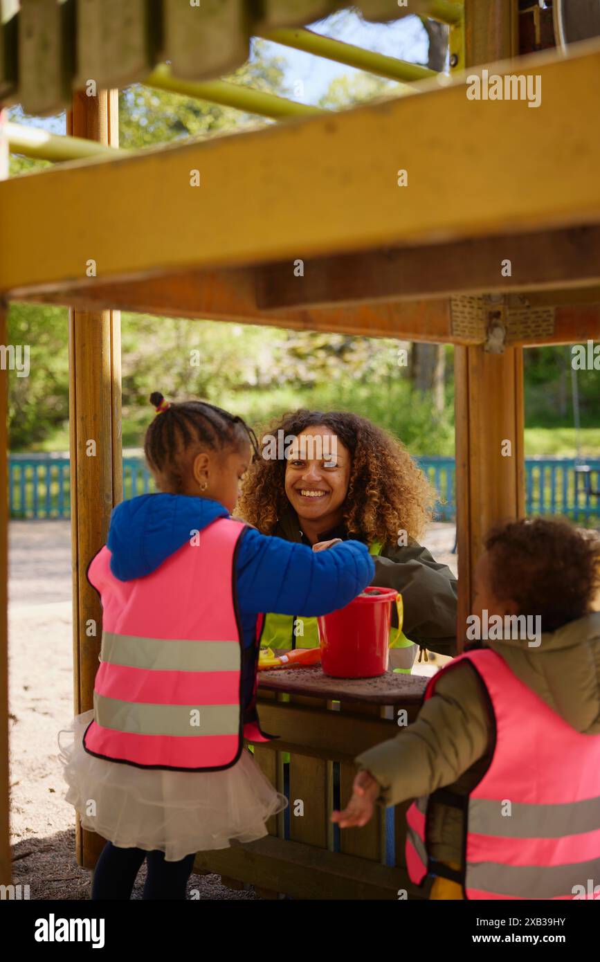 Girls wearing reflective vests playing with happy mother at playground ...