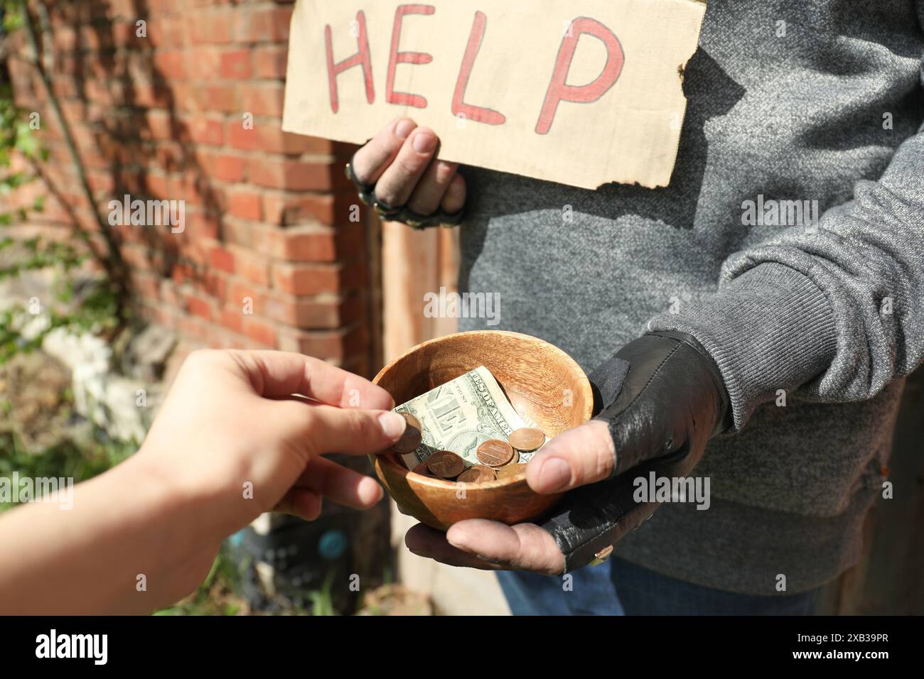 Woman giving money to poor homeless man with Help sign outdoors, closeup. Charity and donation ...