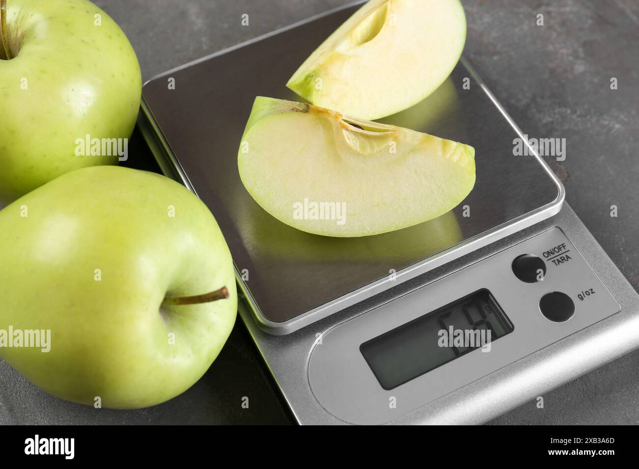 Kitchen scale with pieces of apple and fruits on grey textured table ...