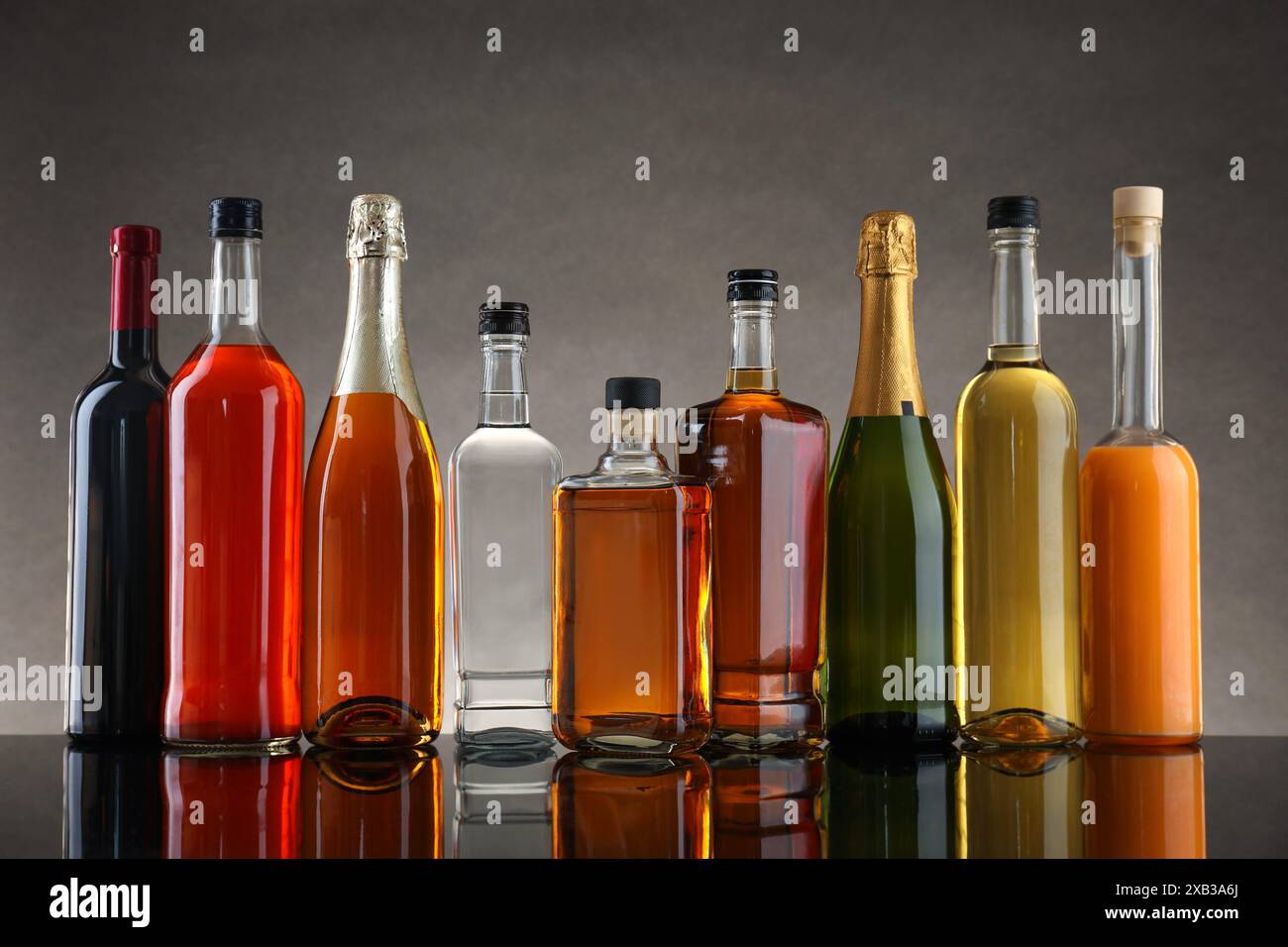 Bottles of different alcoholic drinks on table against gray background ...