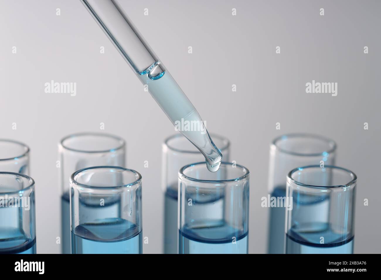 Dripping light blue liquid from pipette into test tube on gray ...