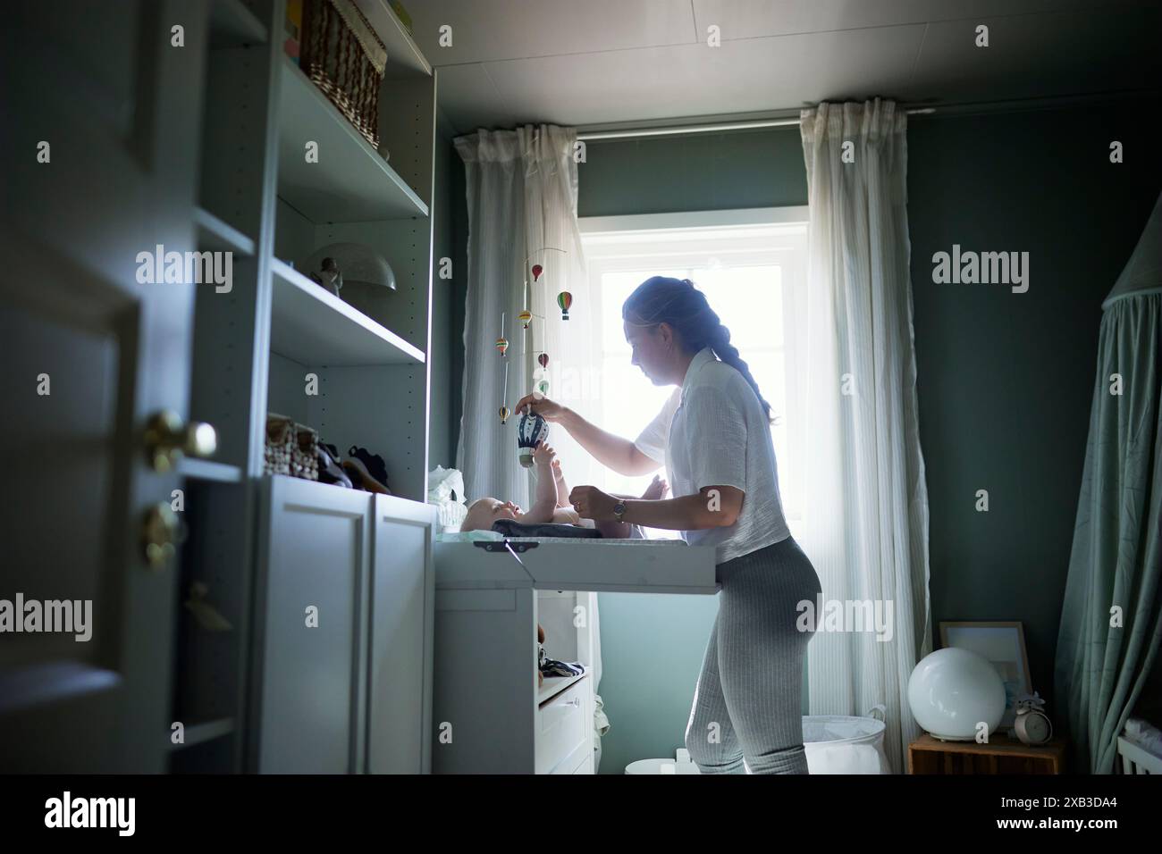 Side view of mother changing baby's diaper while standing by window ...