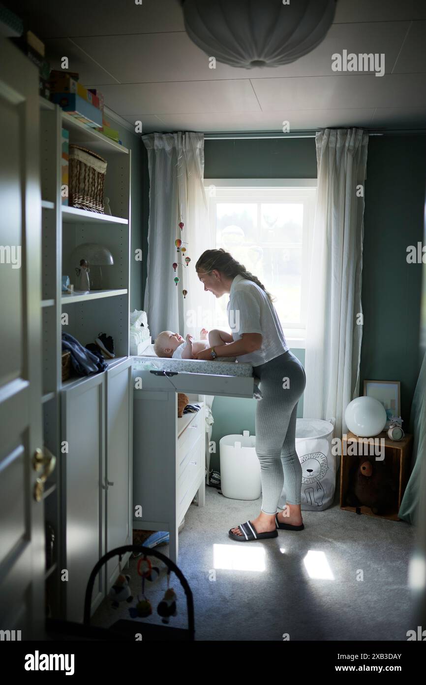 Full length side view of mother changing baby's diaper while standing ...
