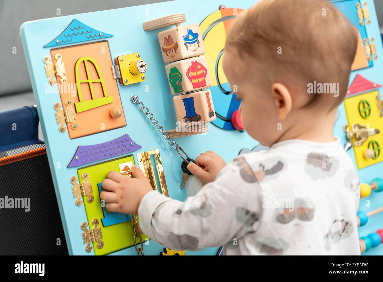 A toddler uses a key for a small lock while playing with a busy board ...