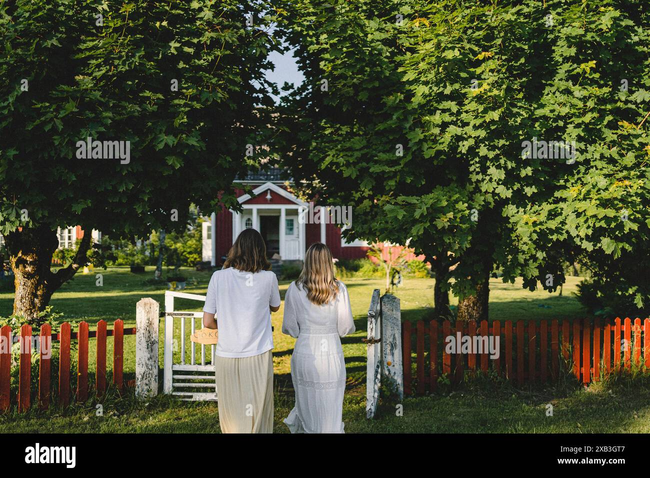 Rear view of young women walking towards gate near house and trees ...