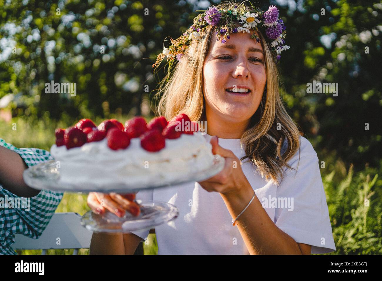 Smiling young blond woman wearing tiara holding cakestand during brunch ...