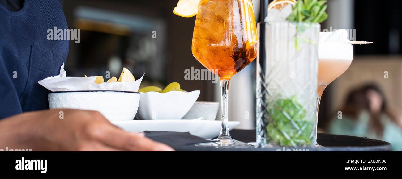 Waiter serving refreshing cocktails and snacks on a tray in a stylish ...
