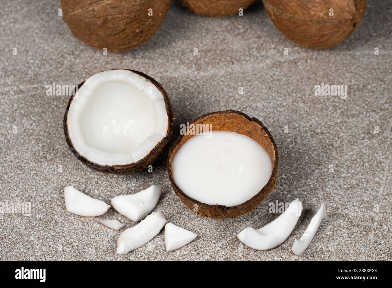 Coconut milk in coconut shell and half coconut, chopped flesh on grey ...