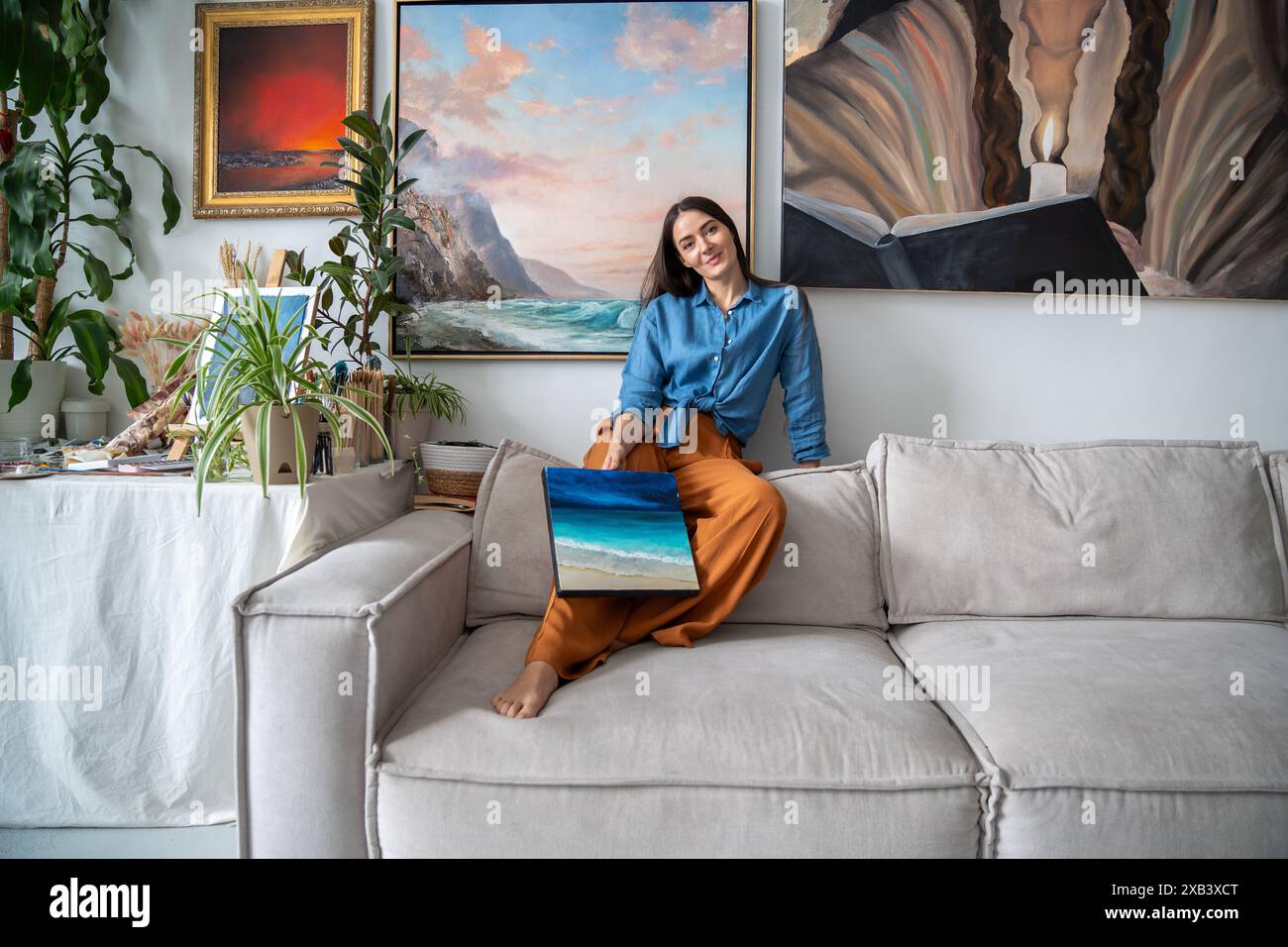 Creative satisfied female artist demonstrates picture, relaxed sitting ...