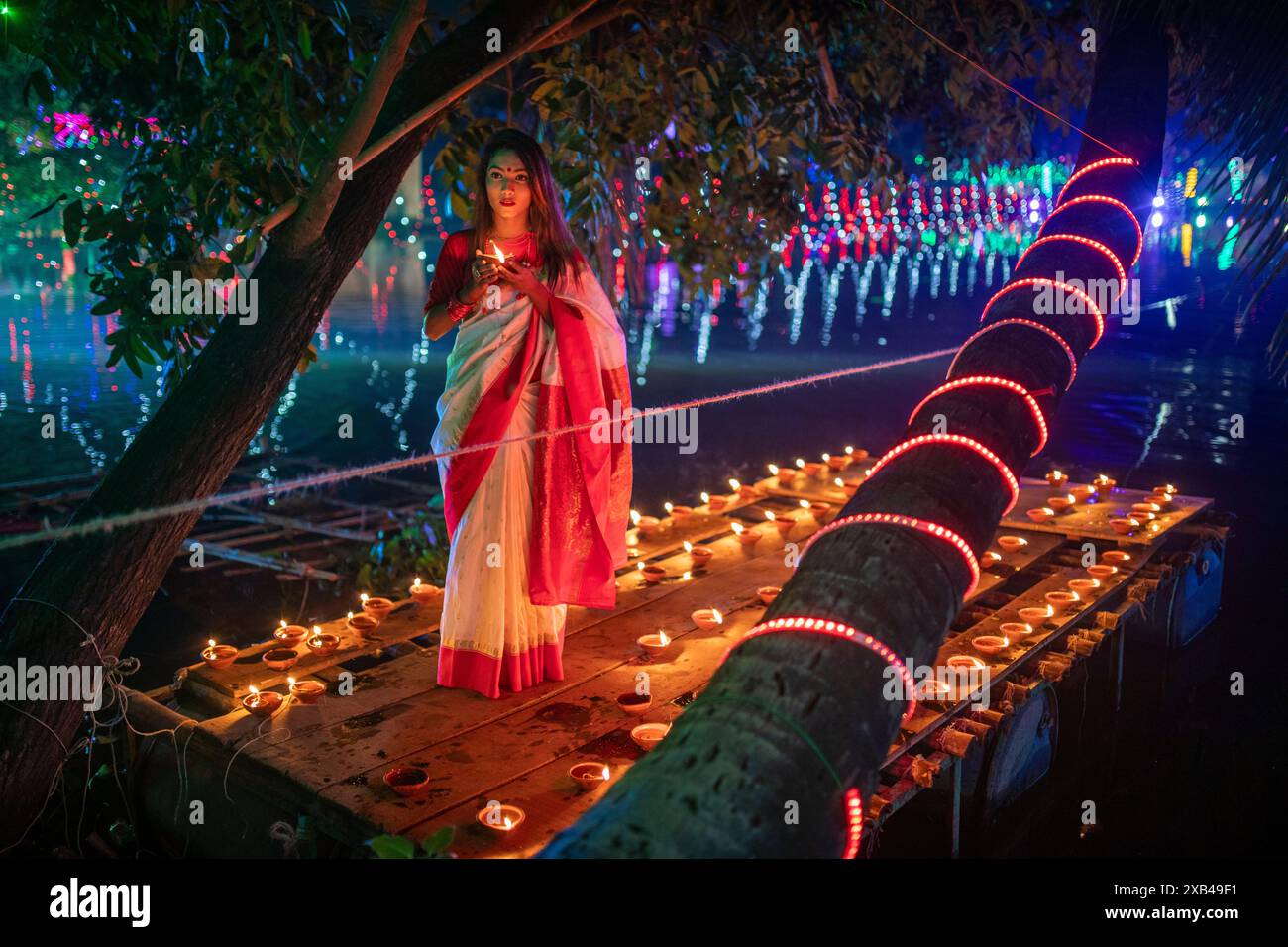A young woman illuminates Diwali lamps at the pond of Sri Sri ...