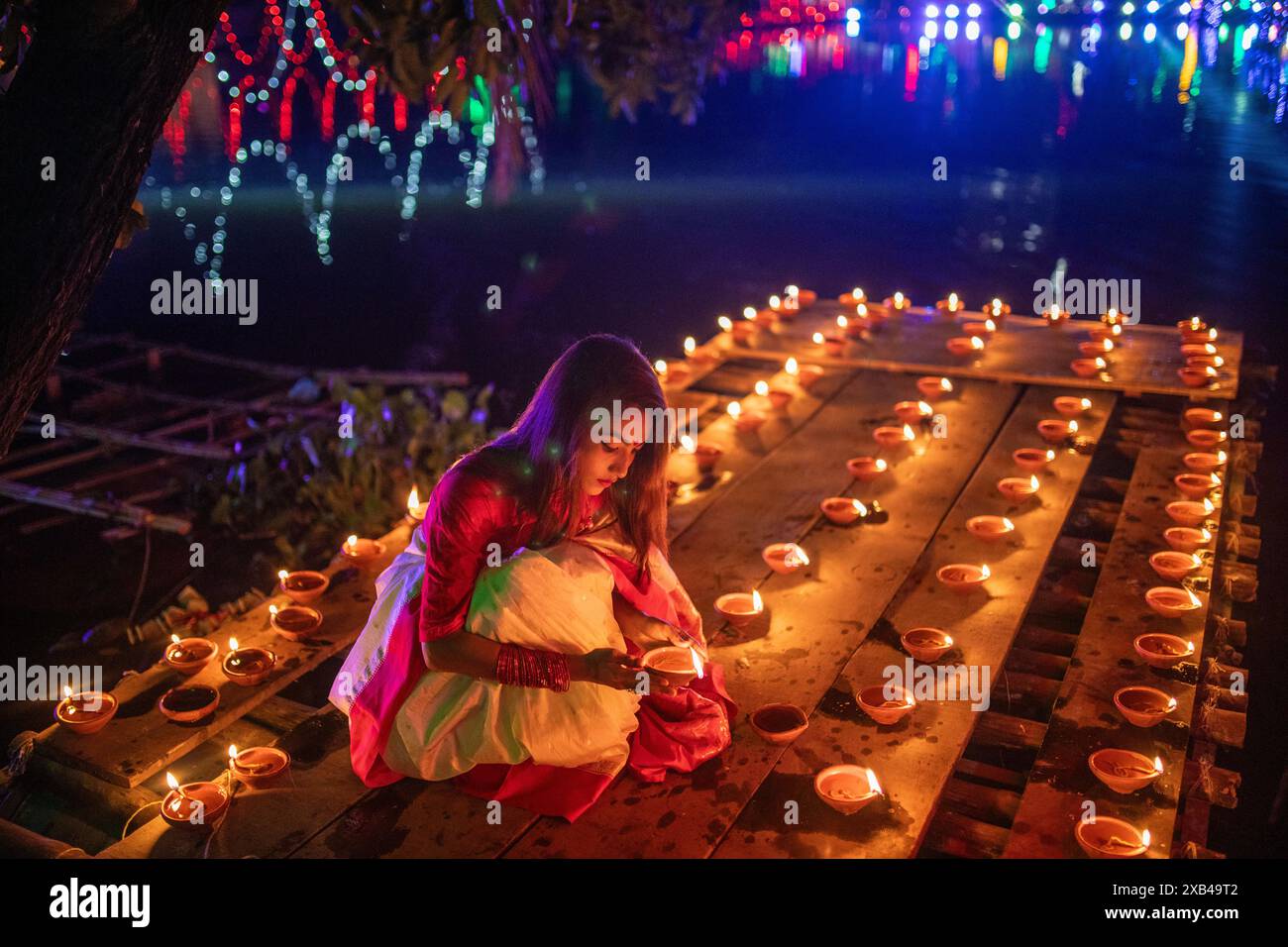 A young woman illuminates Diwali lamps at the pond of Sri Sri ...