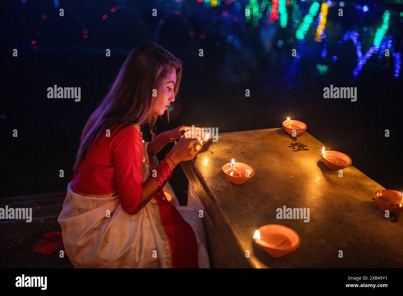 A young woman illuminates Diwali lamps at the pond of Sri Sri ...