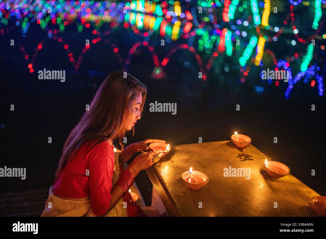 A young woman illuminates Diwali lamps at the pond of Sri Sri ...