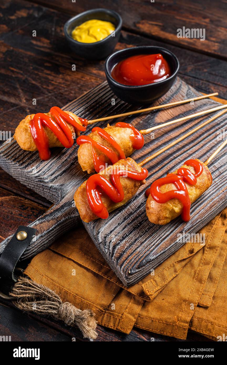 Mini Deep fried corn dogs with mustard and ketchup on wooden board ...