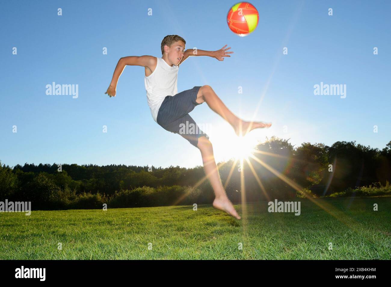 A boy jumping in the air about to kick a soccer ball on a grassy field ...
