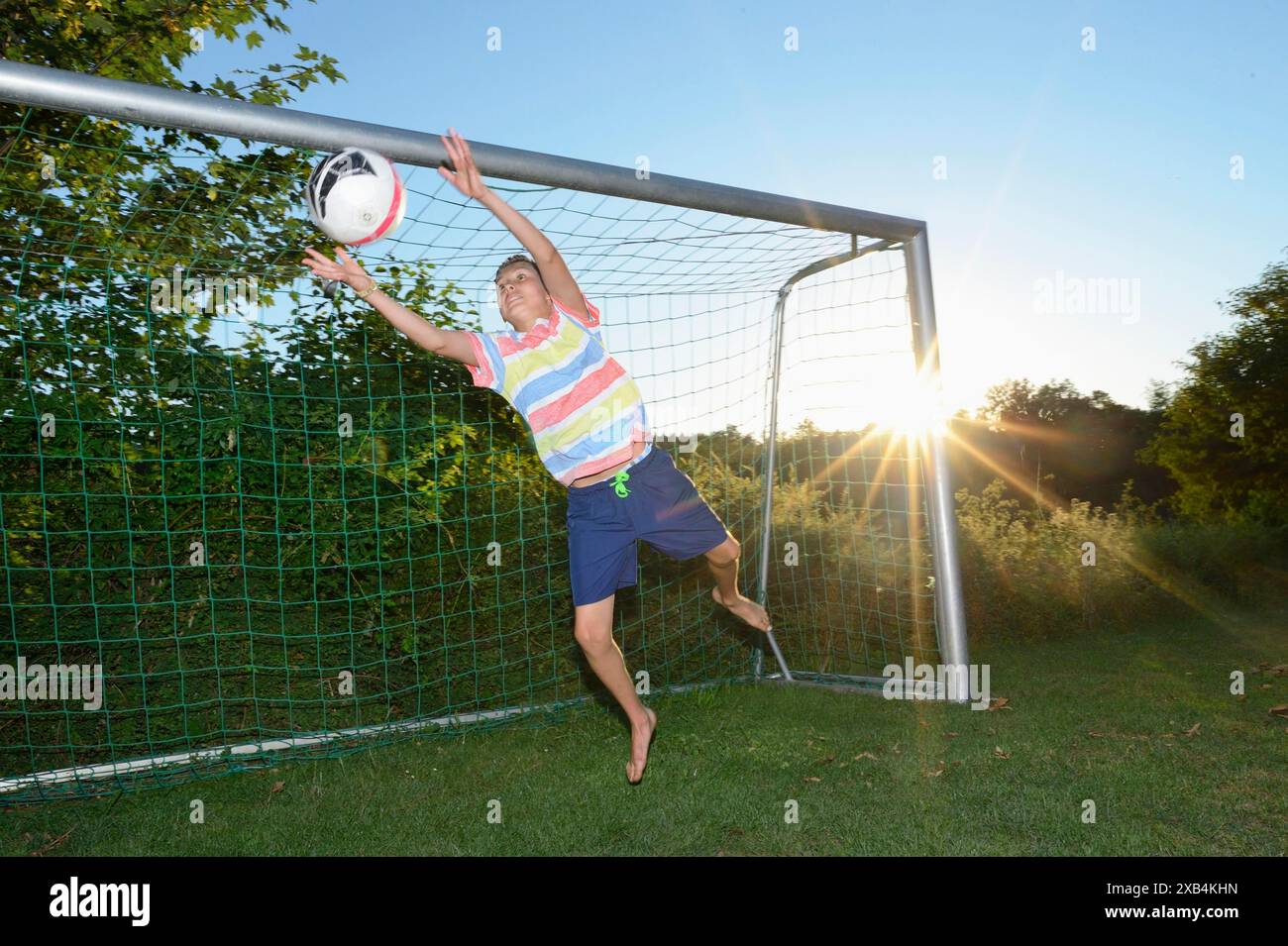 A boy jumping to save a soccer ball as a goalkeeper, with the sun ...