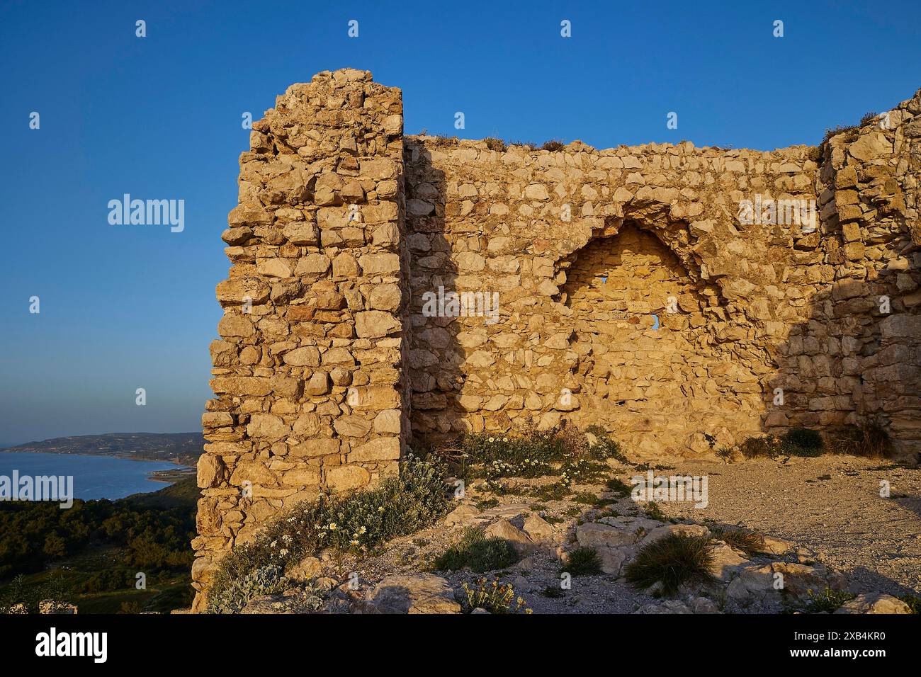 A historic stone ruin on a hill overlooking the sea and vegetation ...