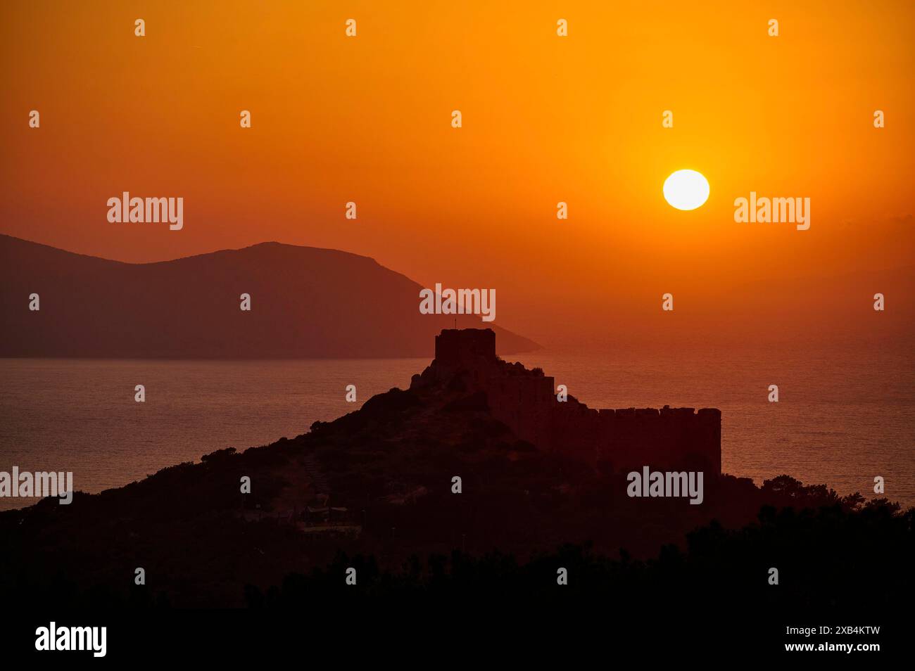 Castle ruins in silhouette against a dramatic sunset over the sea and ...