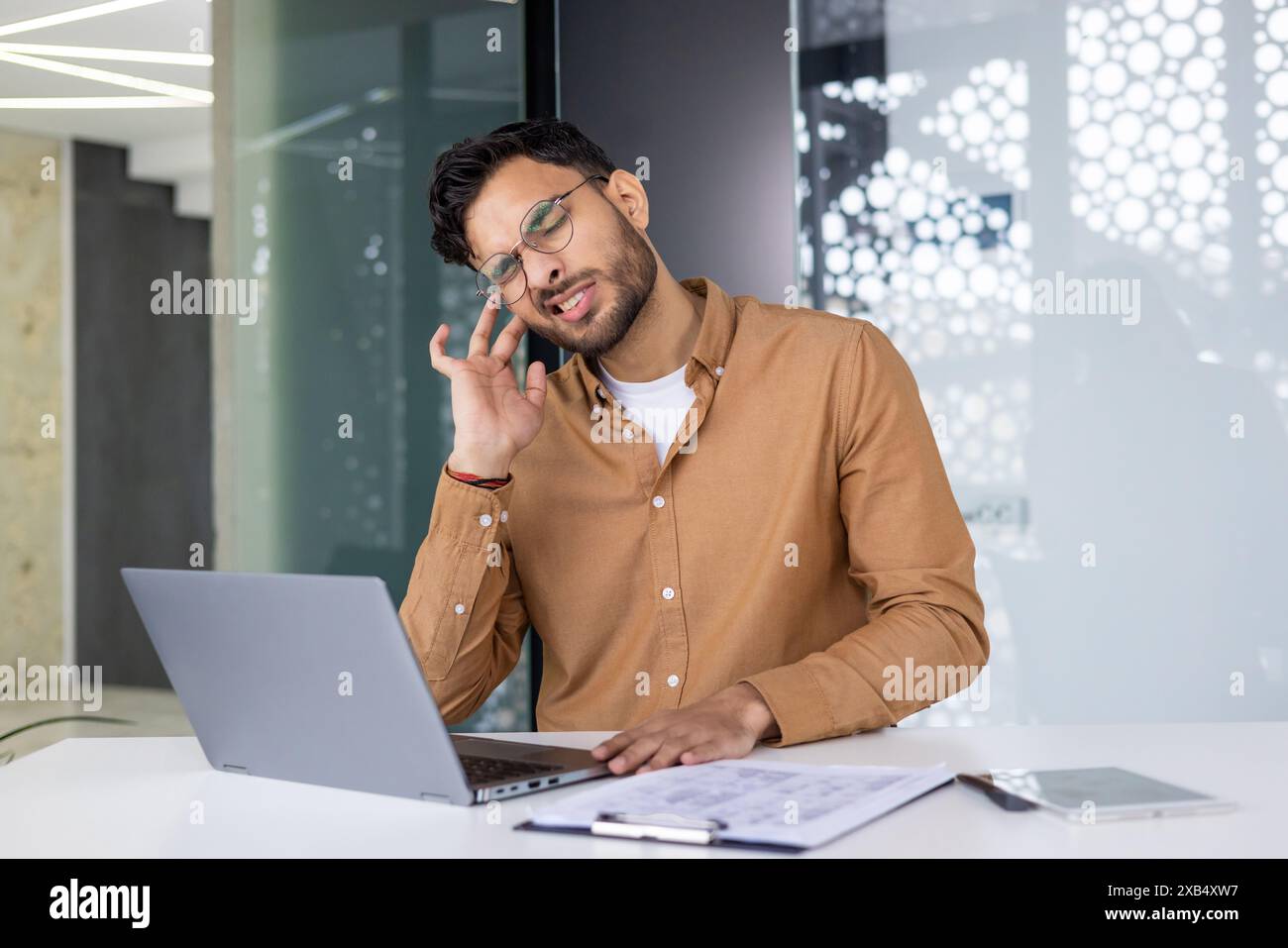 Indian young man hiding in pain, holding hand to ear, sitting at desk ...