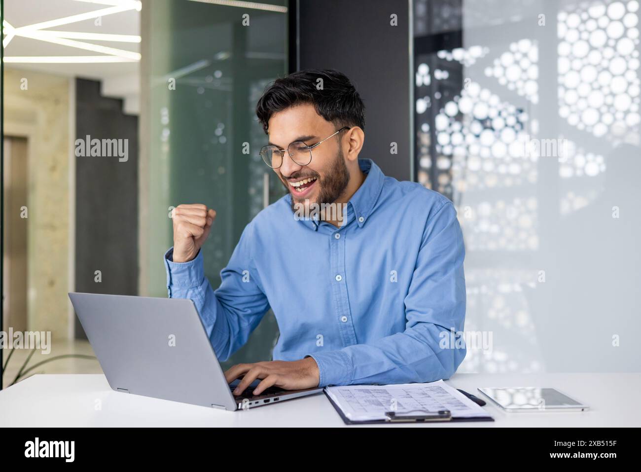 Happy young Indian man working in the office, sitting with a chair and ...