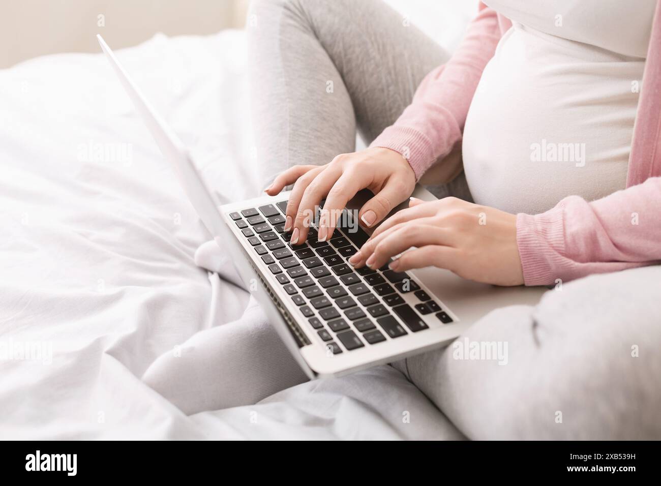Pregnant lady using laptop computer sitting on bed Stock Photo - Alamy