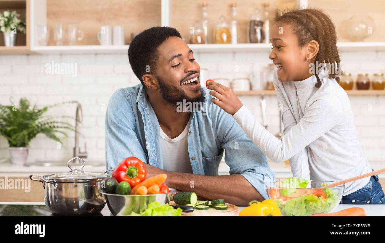 Daughter feeding father vegetable, cooking together at home Stock Photo ...