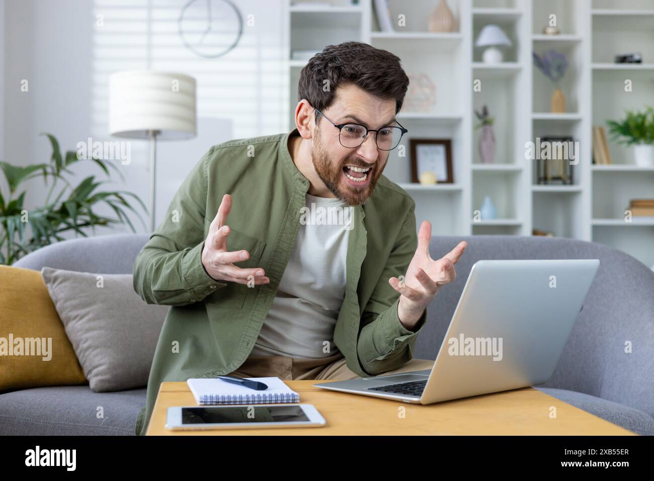 Angry young man in glasses and green shirt sitting on sofa at home in ...