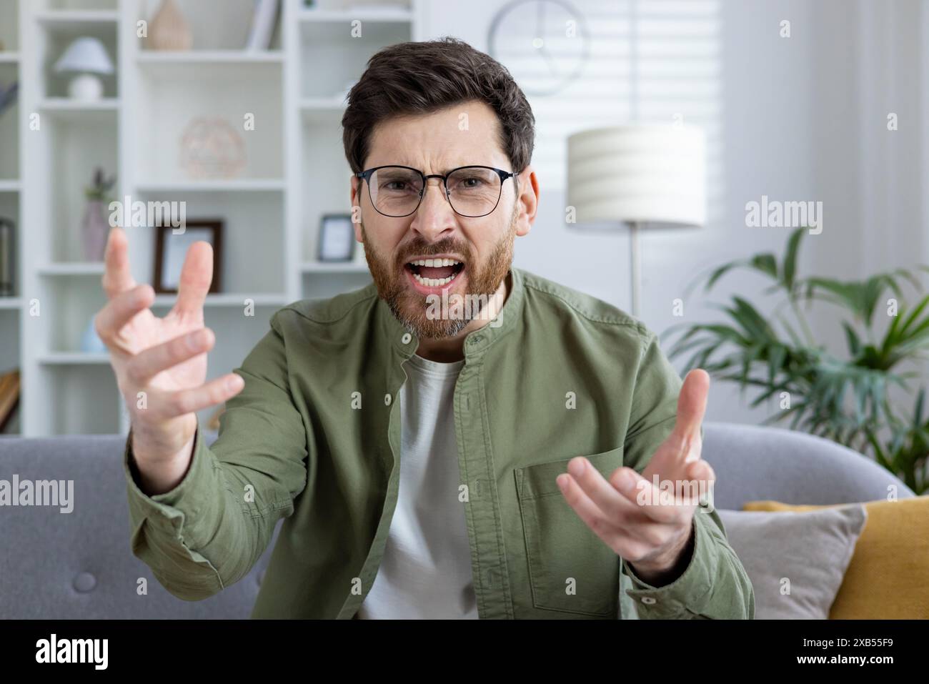 Close-up portrait of angry and worried young man sitting on sofa at ...