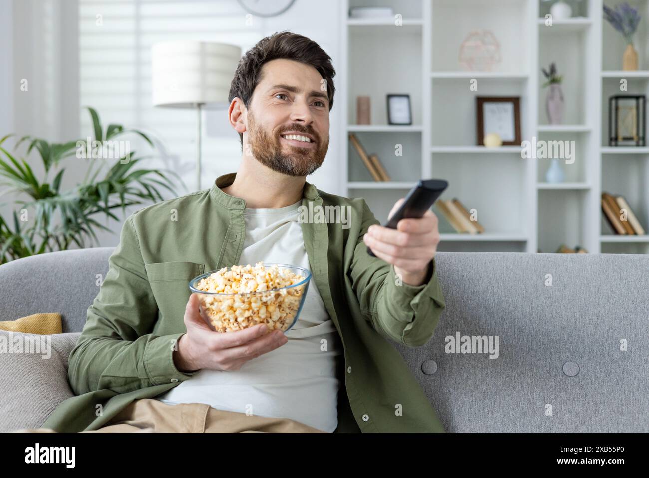 Smiling and relaxed young man sitting on the couch at home and relaxing ...