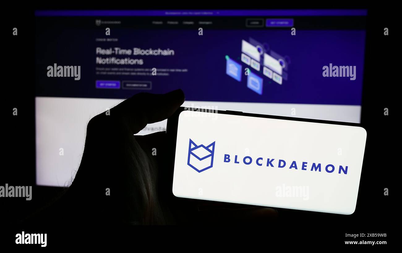 Person holding mobile phone with logo of blockchain software company Blockdaemon Inc. in front ...
