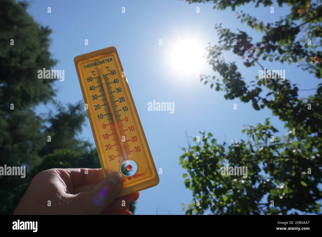 Hand holding thermometer towards the sun and clear sky showing ...